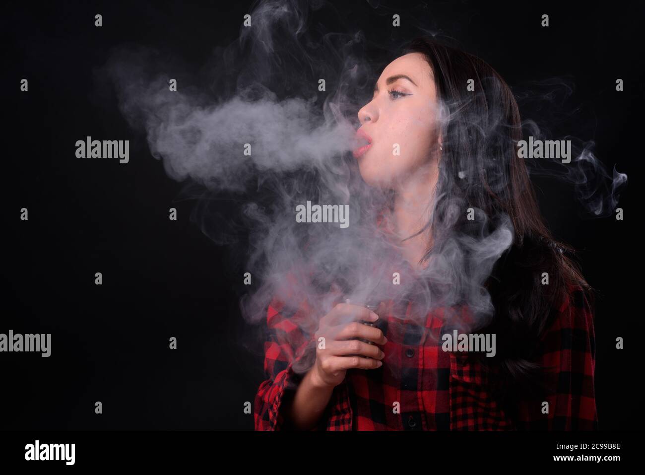Young beautiful Asian woman vaping against black background Stock Photo ...