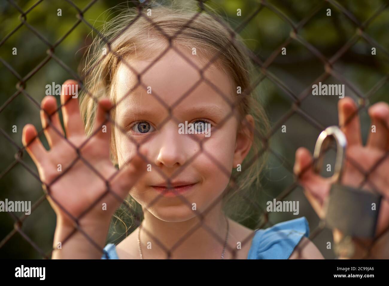 Cute beautiful girl with kind eyes behind bars of a children's shelter ...