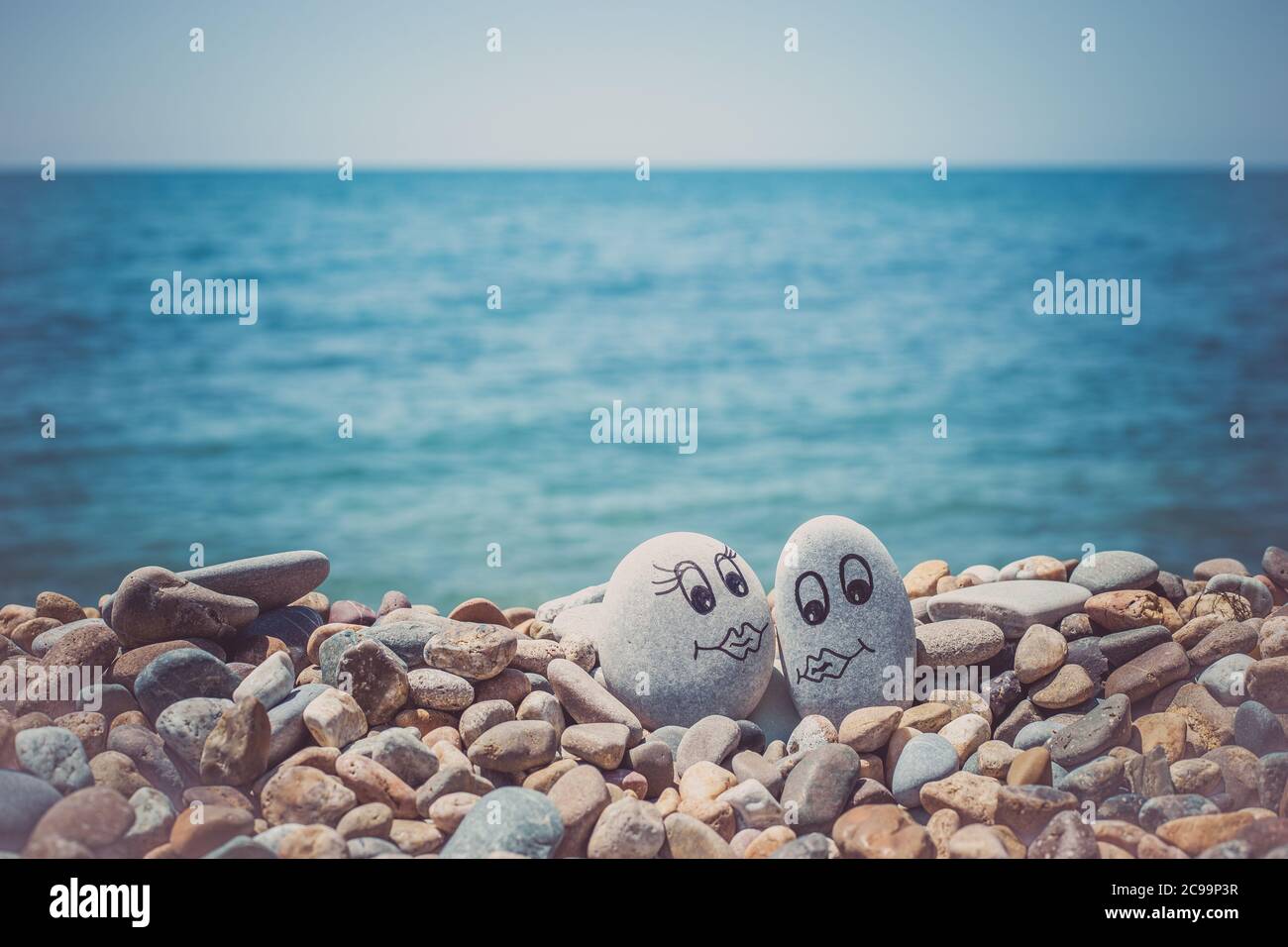 Pebbles with drawn faces in the sand. Loving couple. Travel concept ...