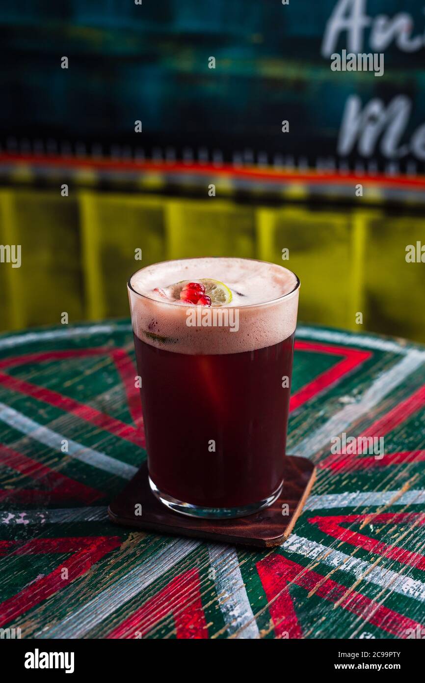 A cocktail in a highball glass with foam, ice cube inside, garnished ...