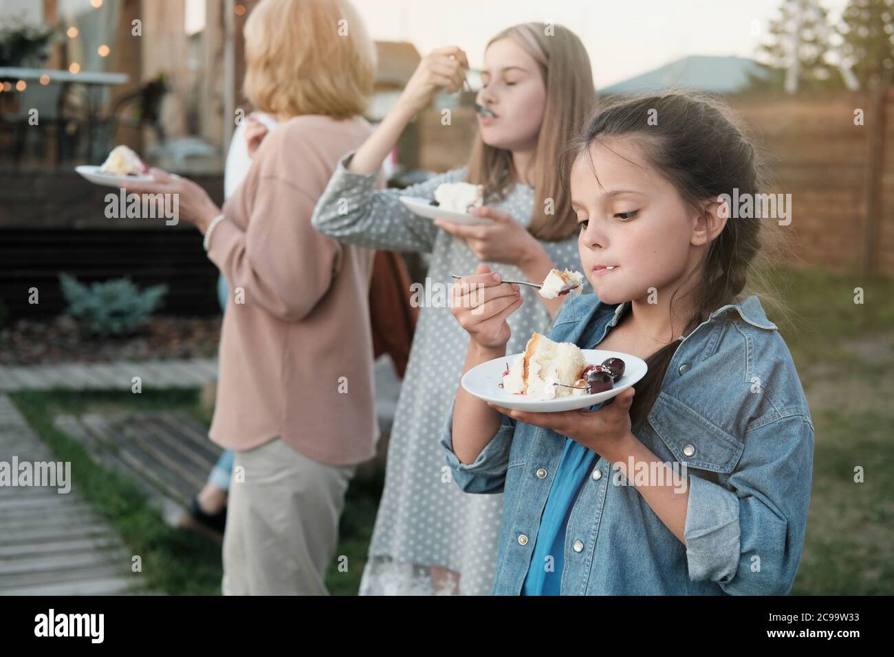 Little girl eating cake while standing with her family in the nature ...