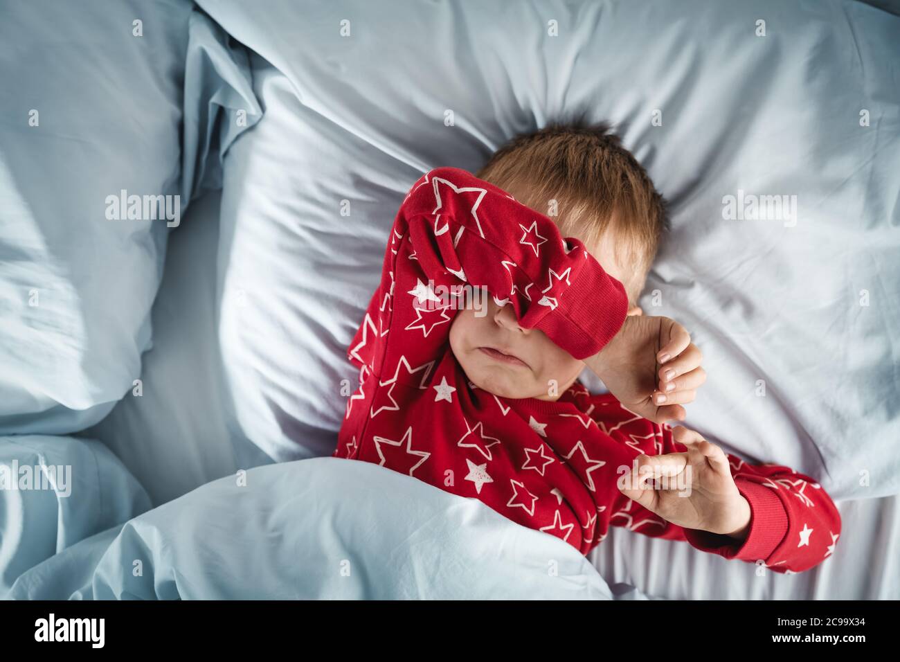 Sleepy boy lying in bed with blue beddings Stock Photo - Alamy
