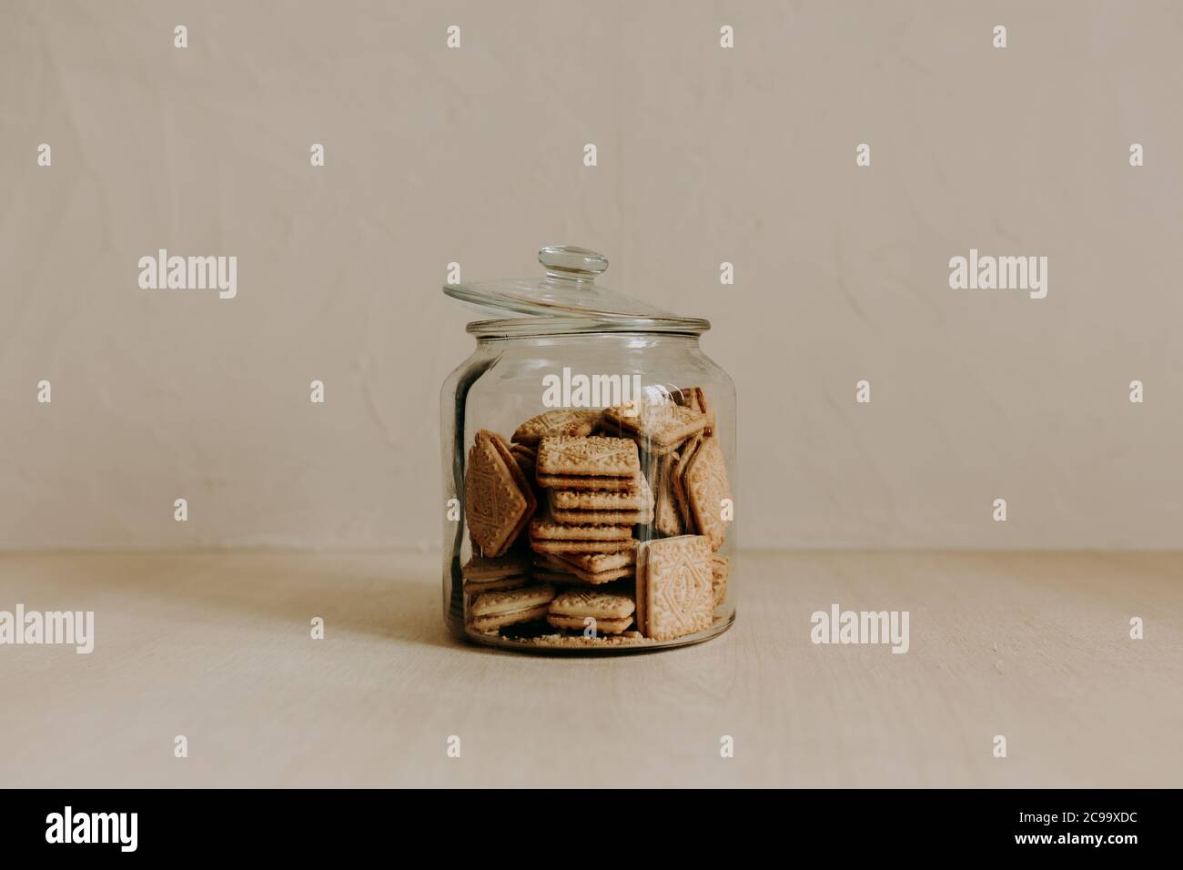 A glass jar of biscuit on wooden table with beige background. The lid ...