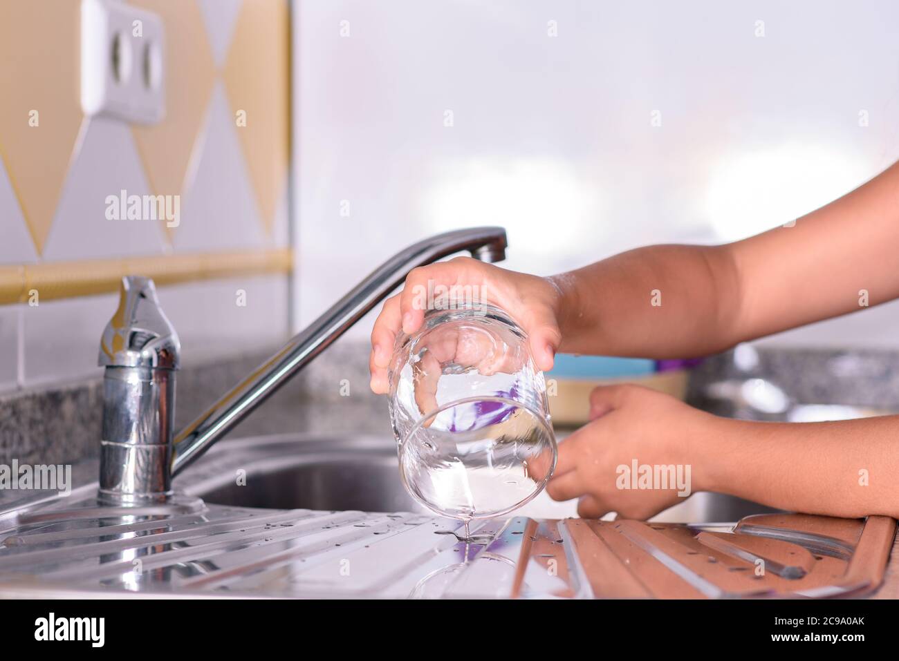 Detail of a girl's wet hands placing a freshly scrubbed glass to dry ...