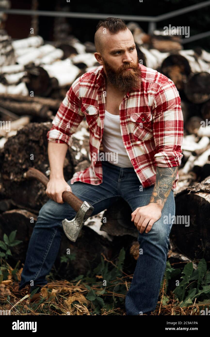 bearded mohawk Man sitting on firewoods. Woodcutter with axe resting ...