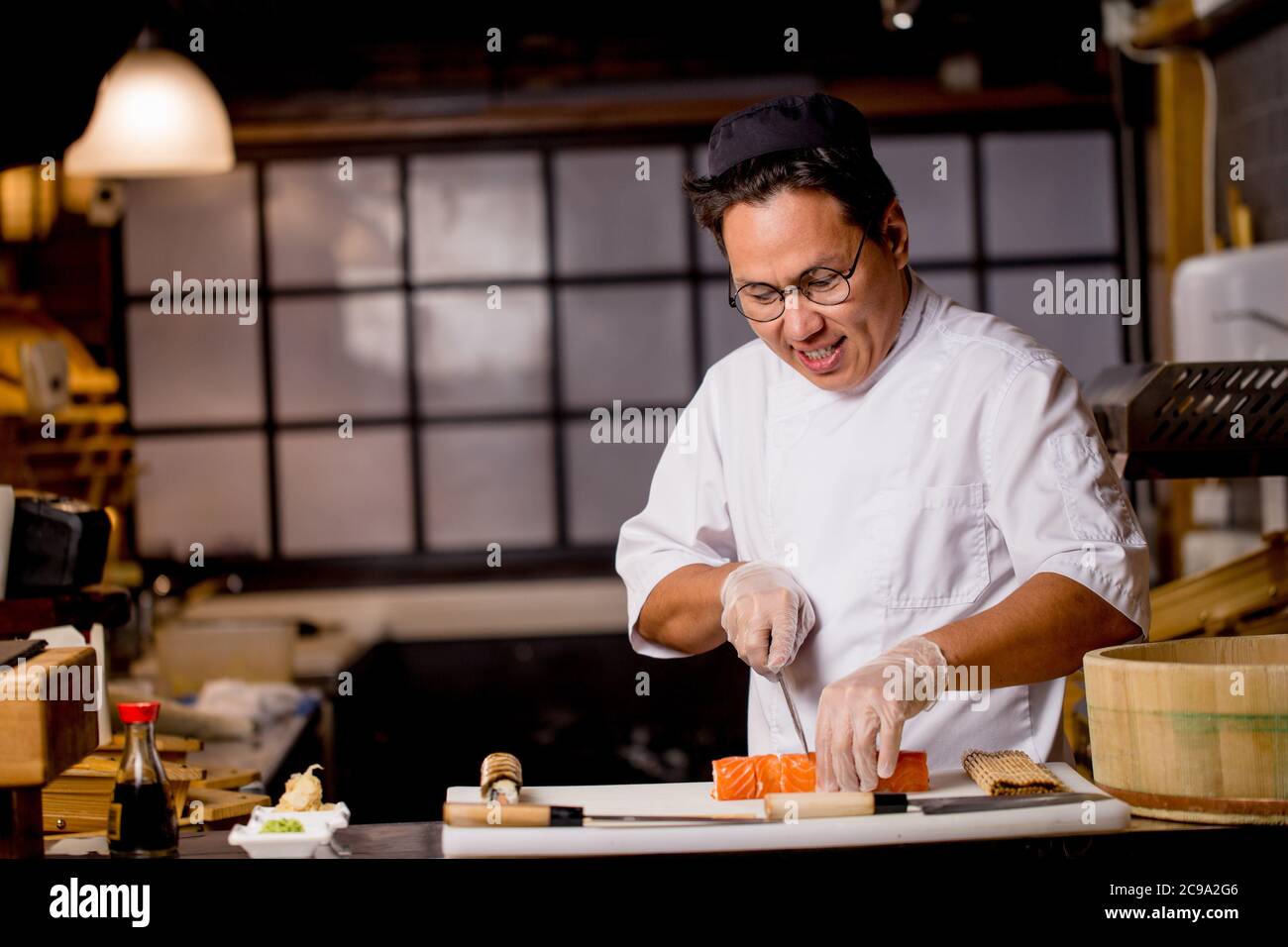 attractive cheerful Asian guy cutting a roll for clients. working hours ...