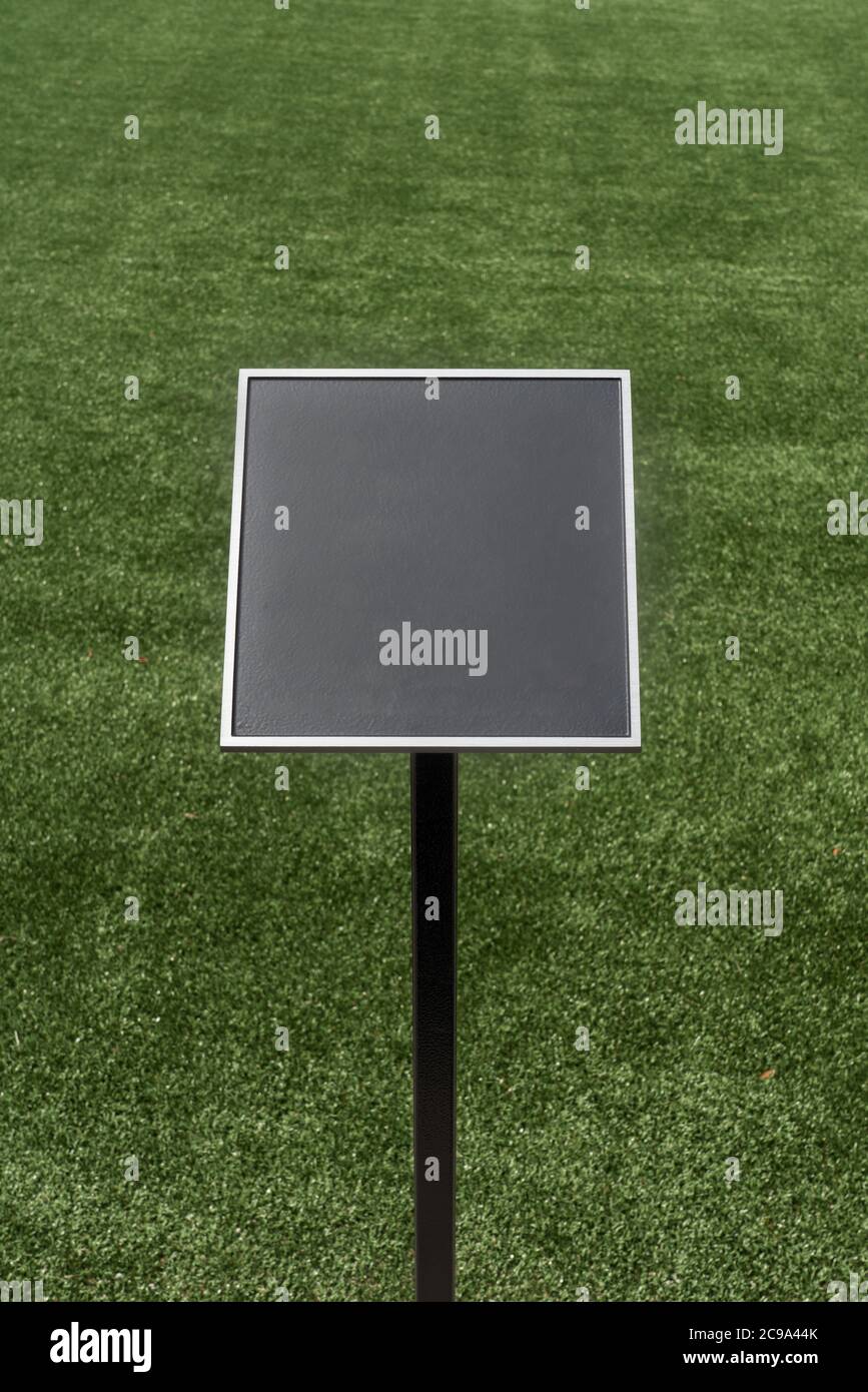 blank grey metal sign on a post in a soft focus green grass background ...