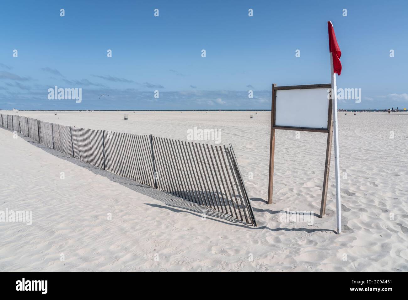blank white sign on white sand beach with storm fencing and red flag ...