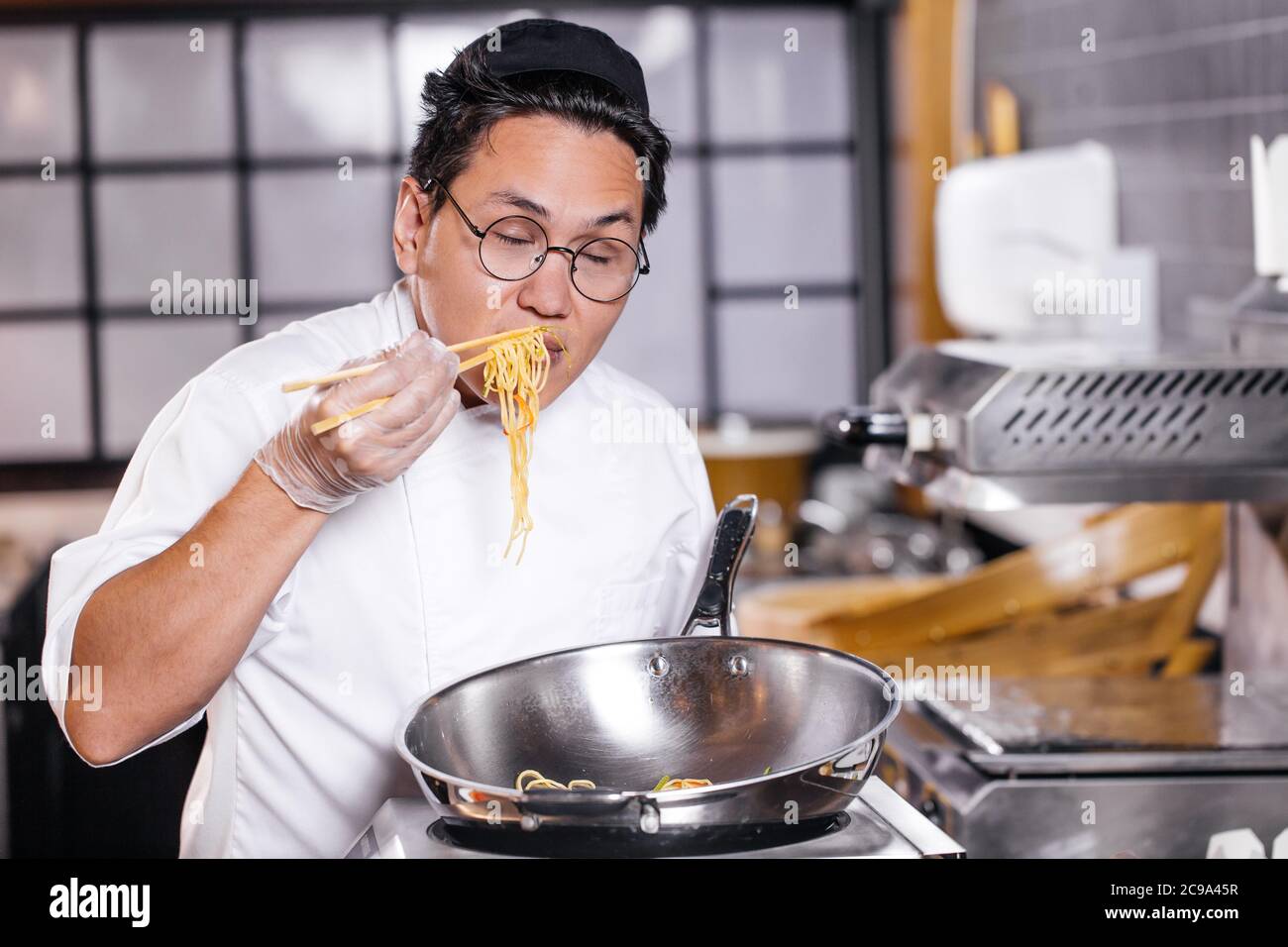 handsome chef with closed eyes eating noodle in the kitchen room. close ...