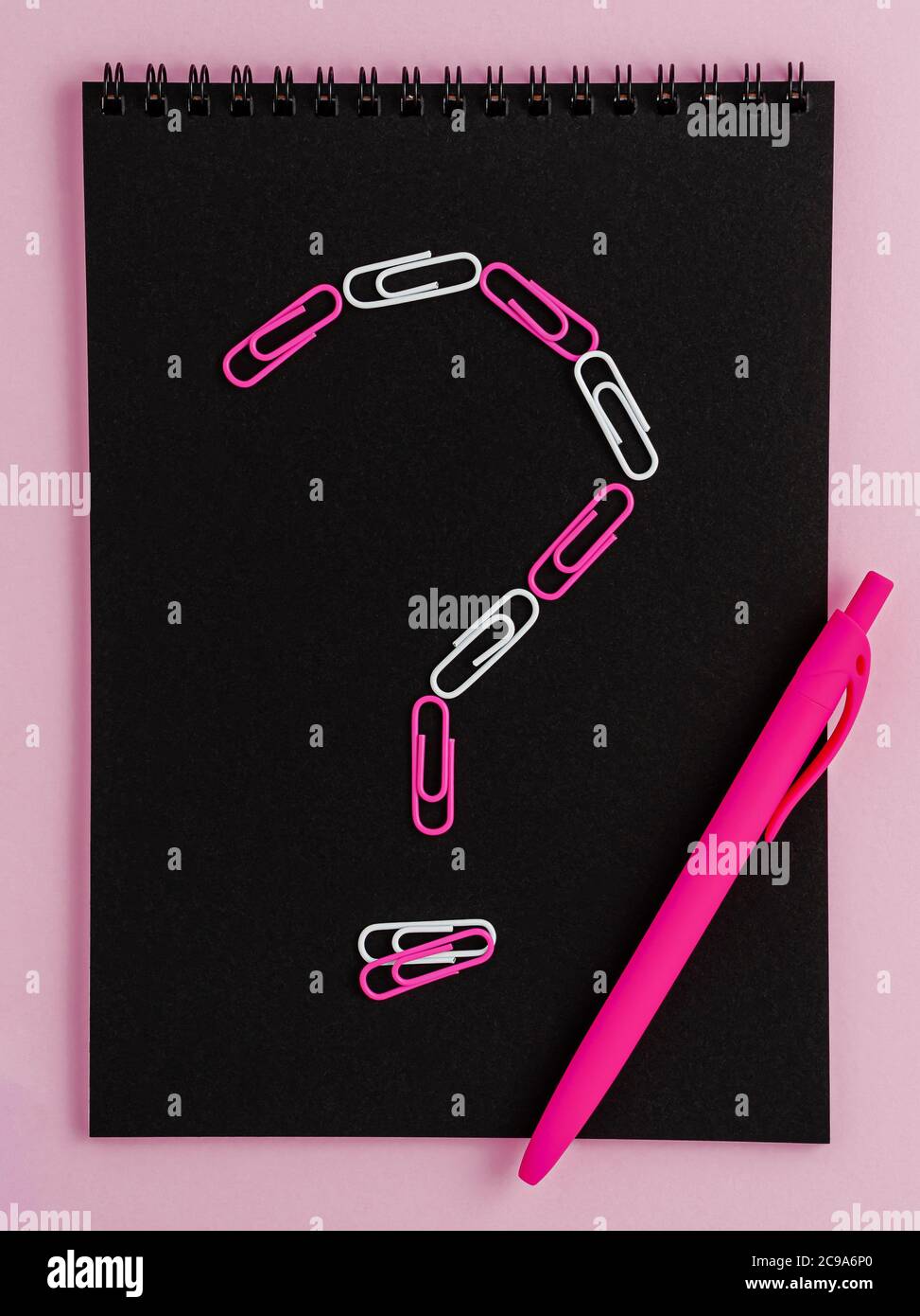 Question mark made of clips on black notebook blank on pink background ...