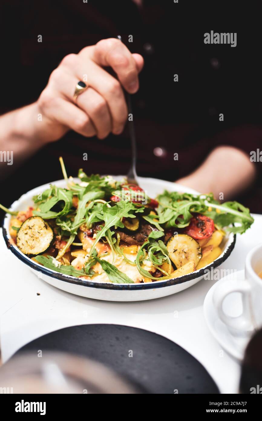 Closeup shot of a woman holding a fork picking her vegetable salad on a ...