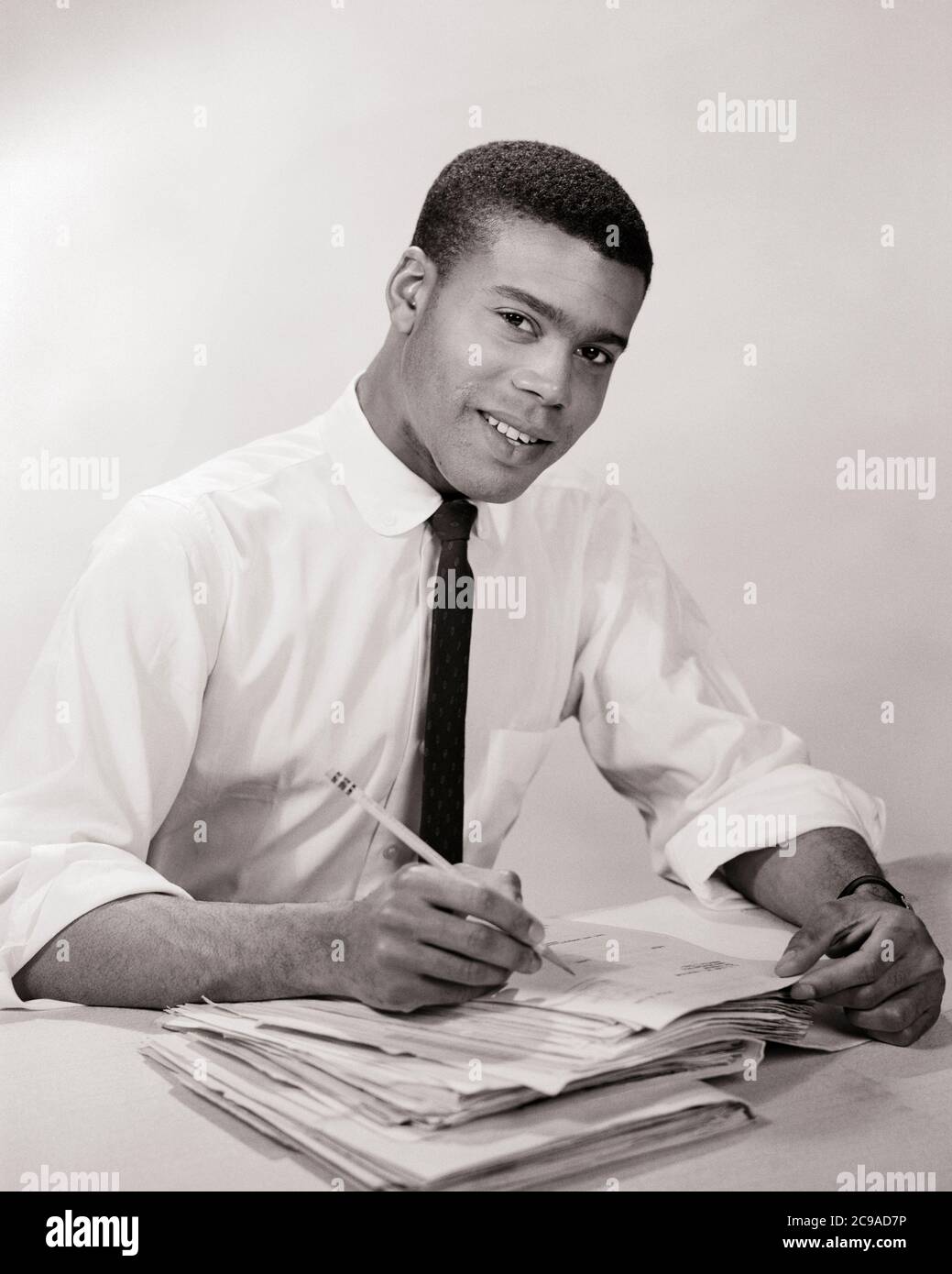 1950s 1960s AFRICAN-AMERICAN MAN HOLDING PENCIL ABOVE PILE OF PAPERWORK ...