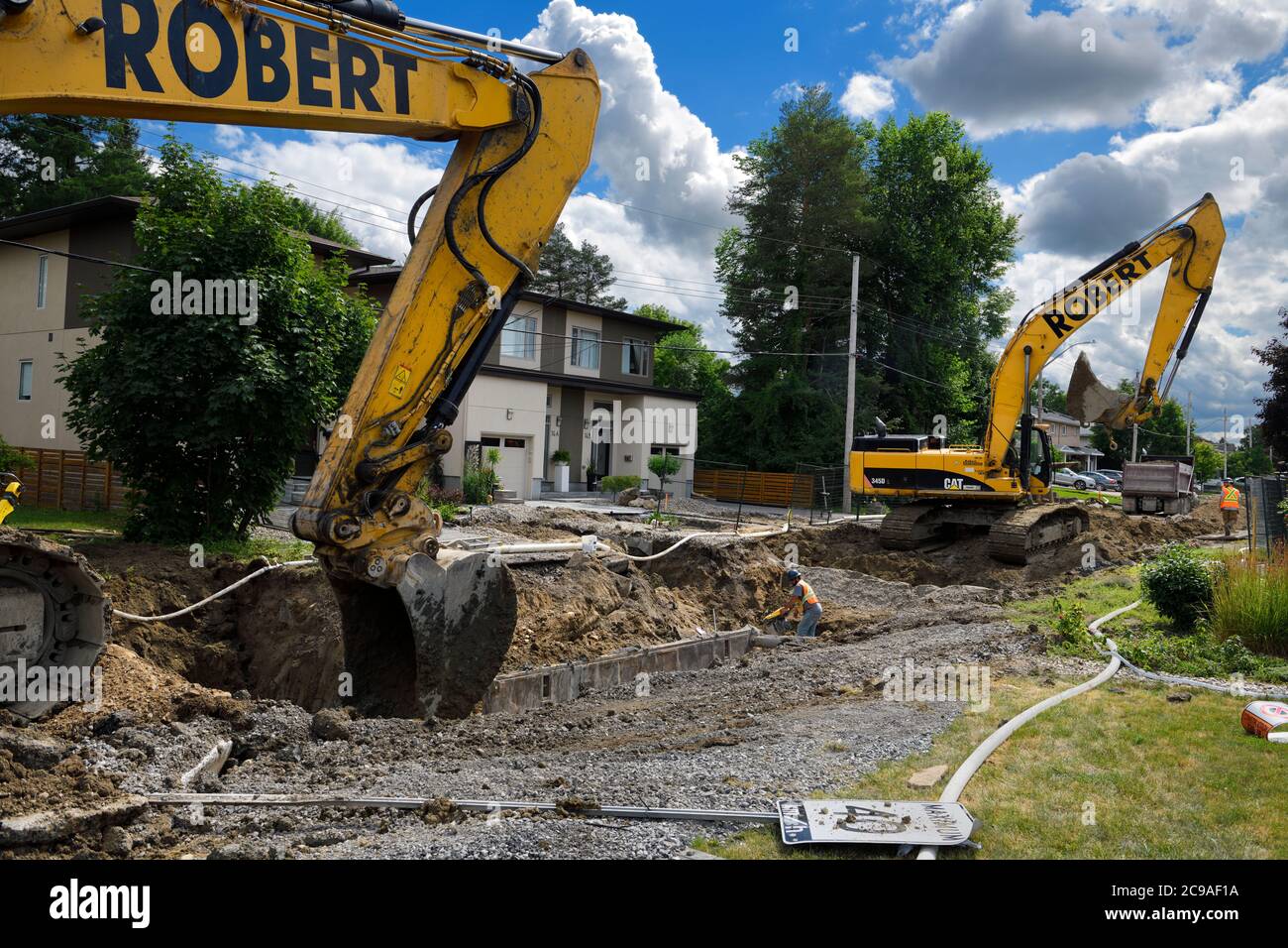 Excavators digging and filling a trench on a residential street in ...