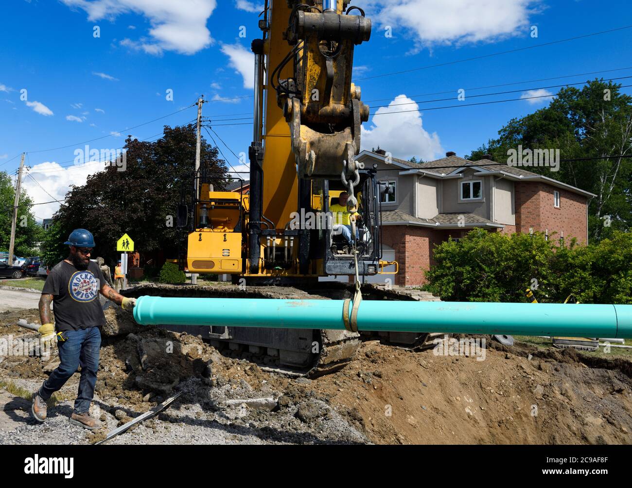 Worker and excavator moving new plastic sewer pipe into trench on ...