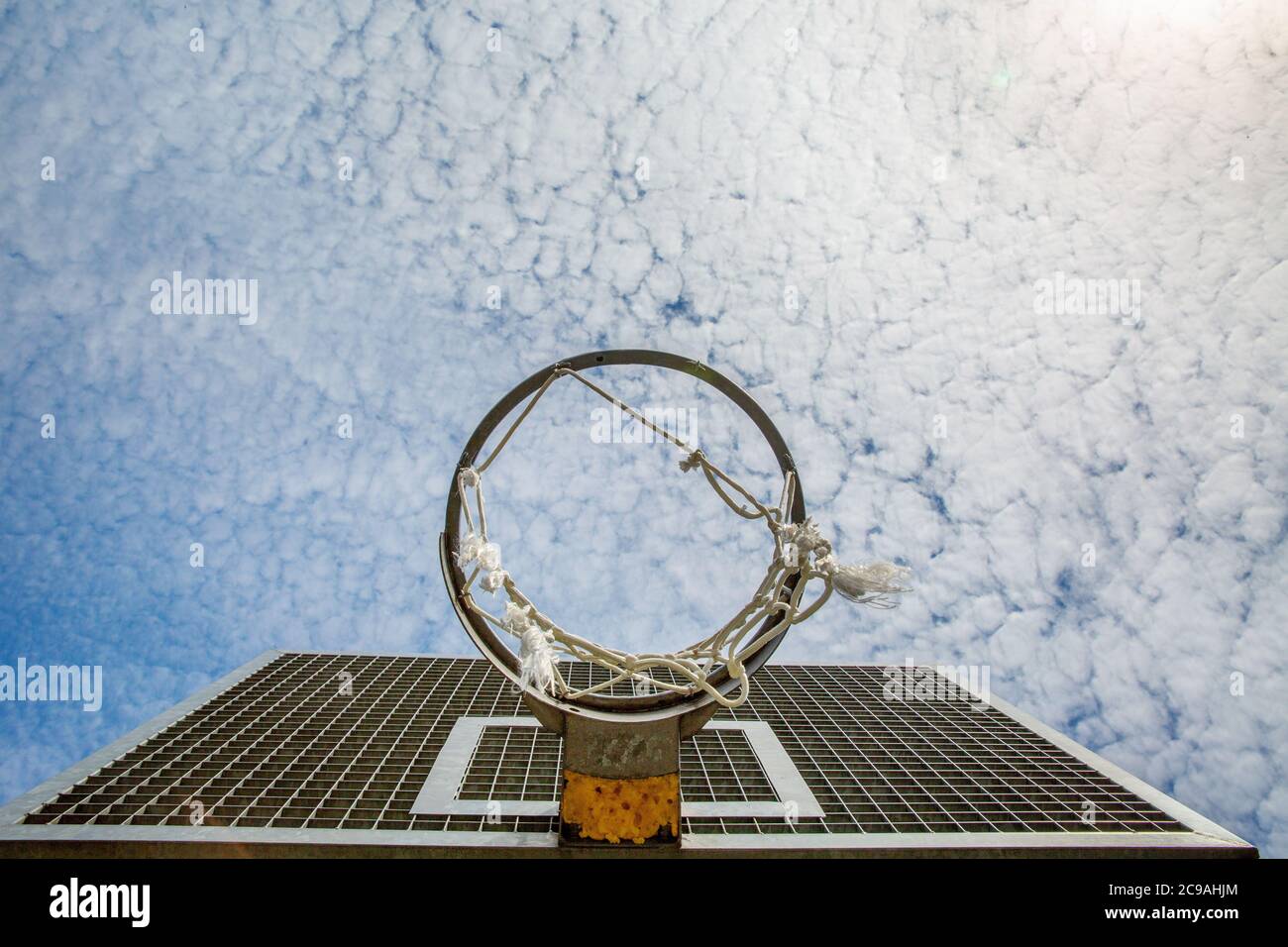 A broken basketball net dangles from a hoop attached to a metal ...