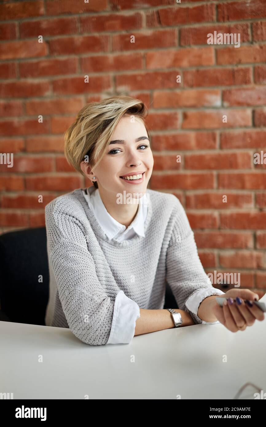 positive blond female secretary at the table in the room with loft ...