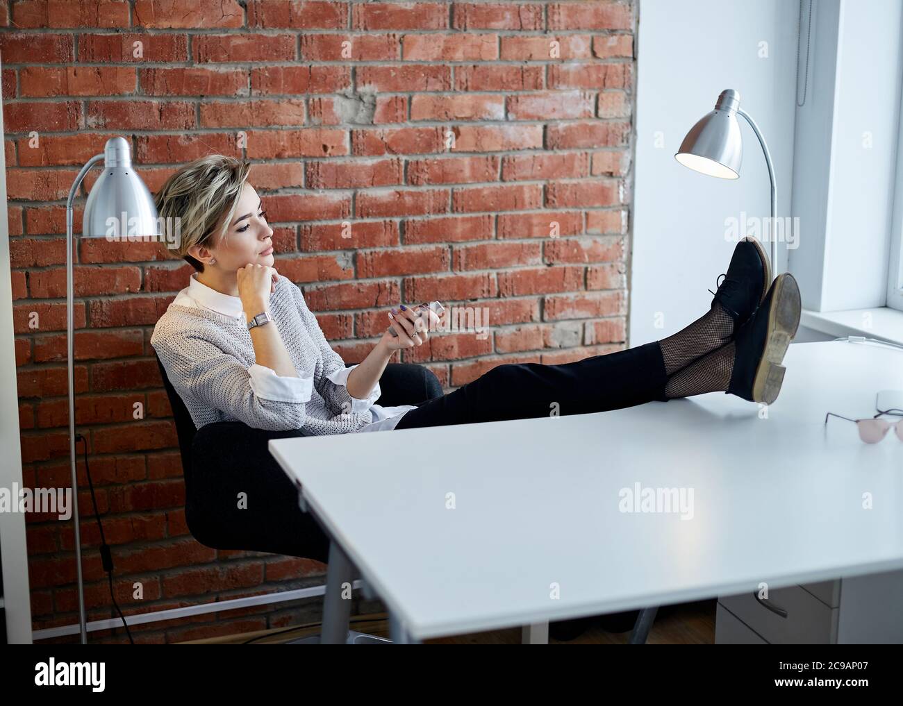 sad blond female boss with her feet on the desk. full length side view ...