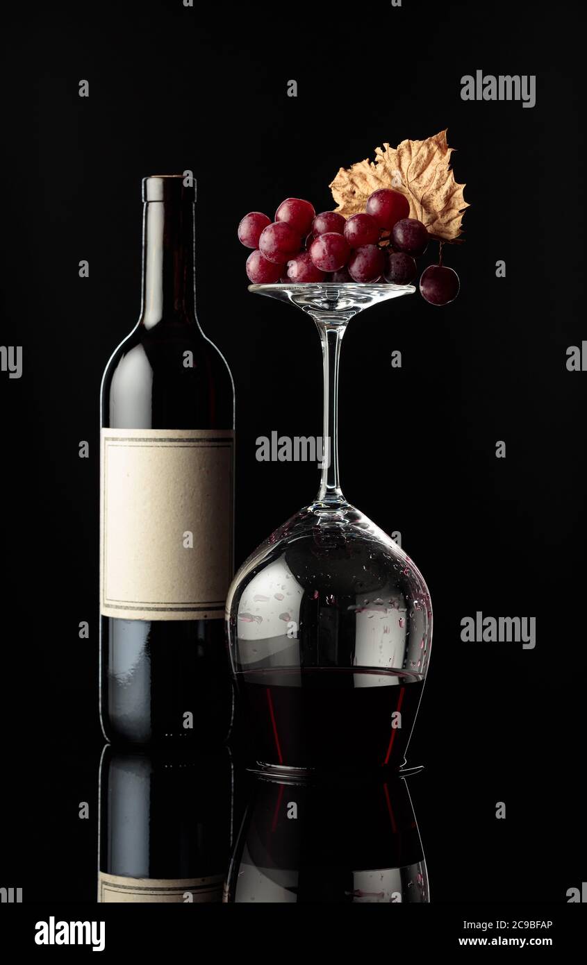 Bottle of red wine and an inverted wine glass with wine on a black ...