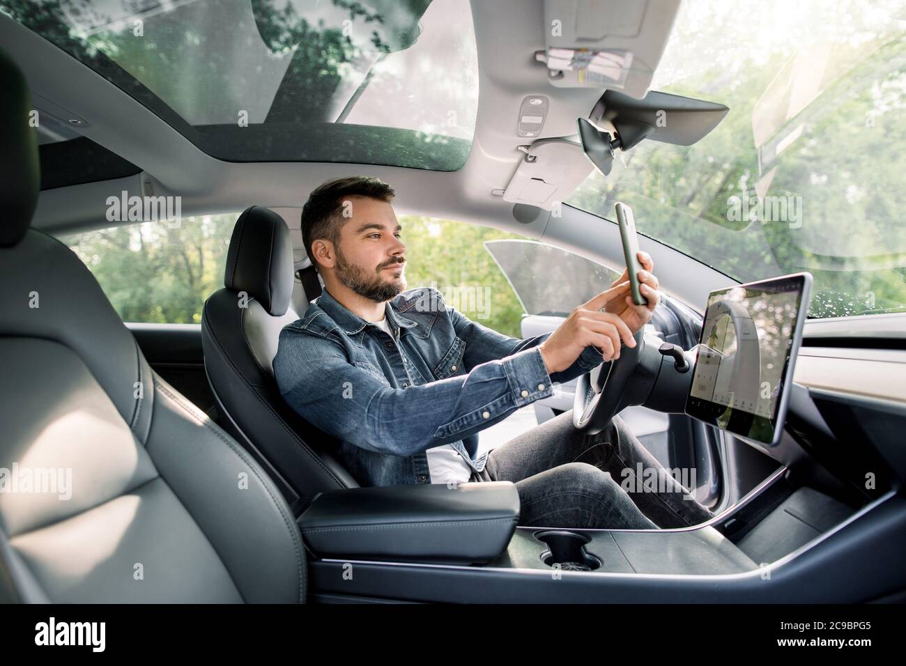 Handsome Caucasian man sitting in modern self-steering electric vehicle ...