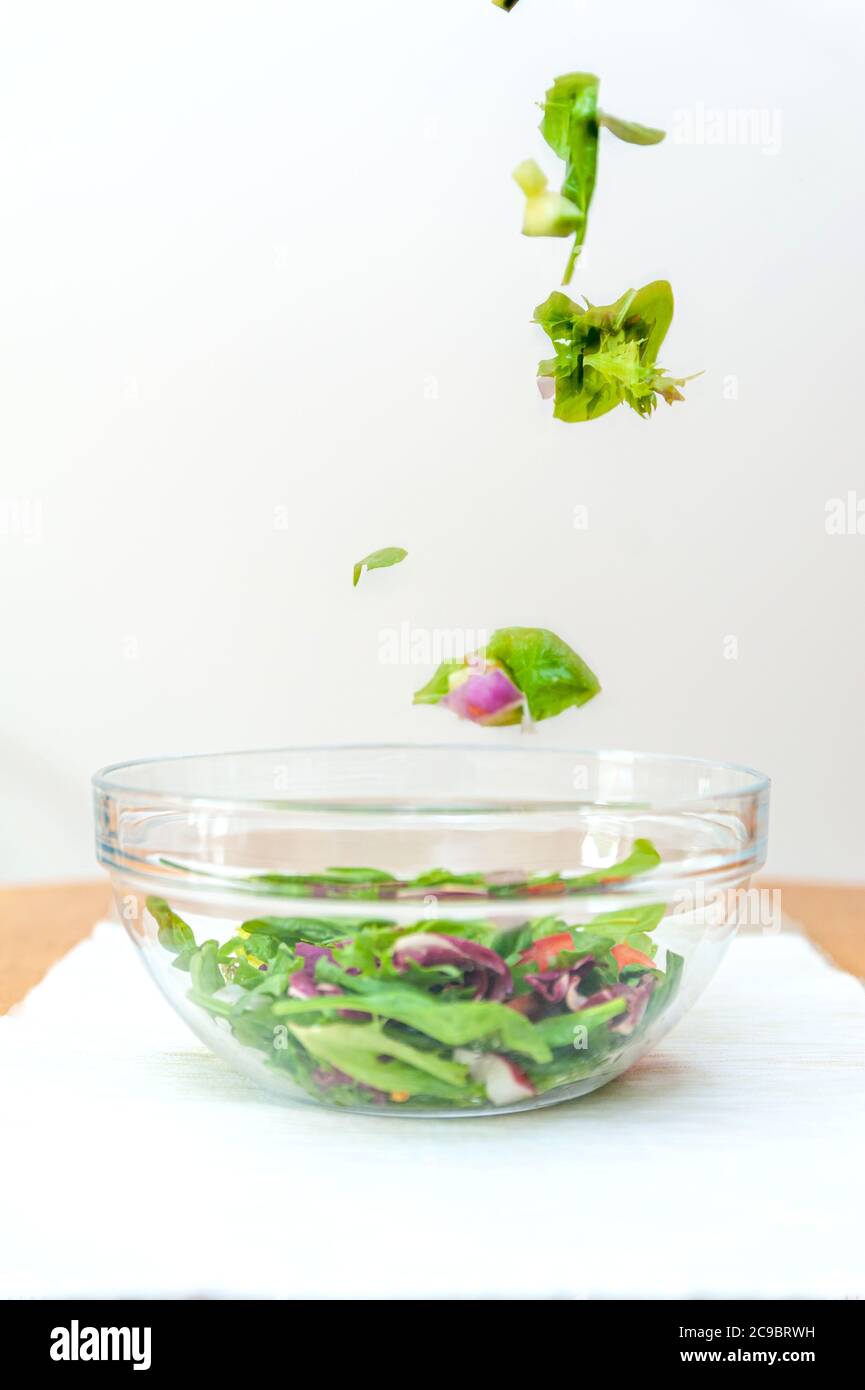 Pieces of fresh vegetables falling down into glass bowl creating ...