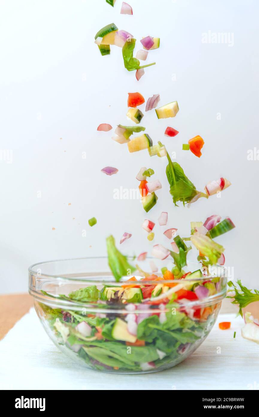 Pieces of fresh vegetables falling down into glass bowl creating ...