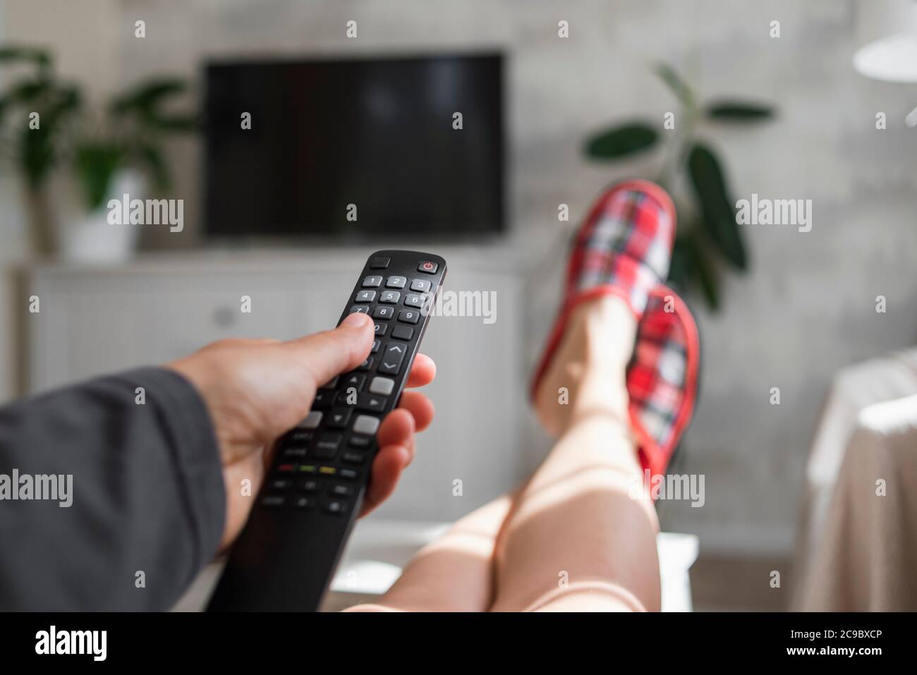 Hand with TV remote control in living room. Watching television. Legs ...