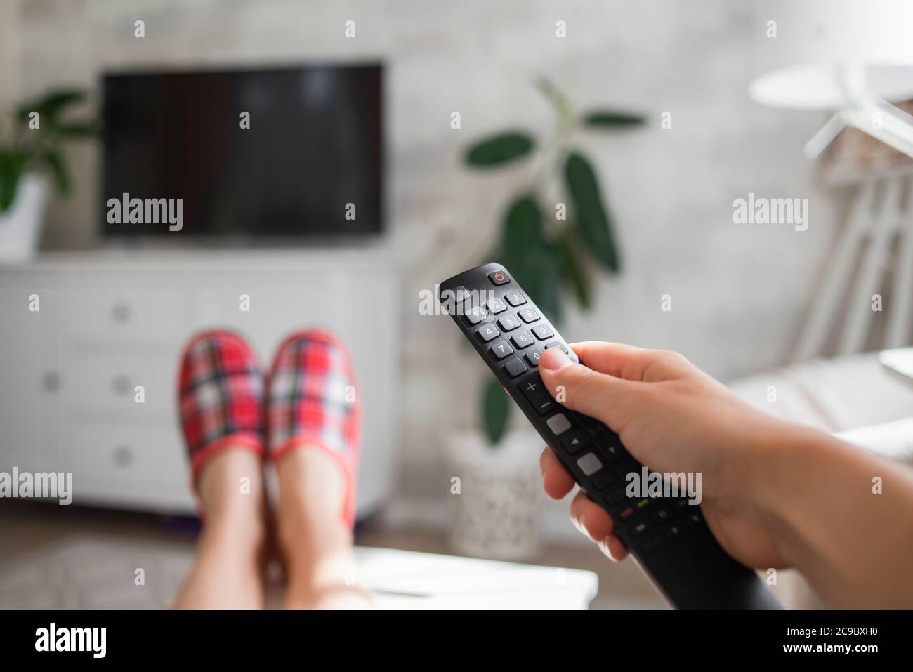 Hand with TV remote control in living room. Watching television. Legs ...