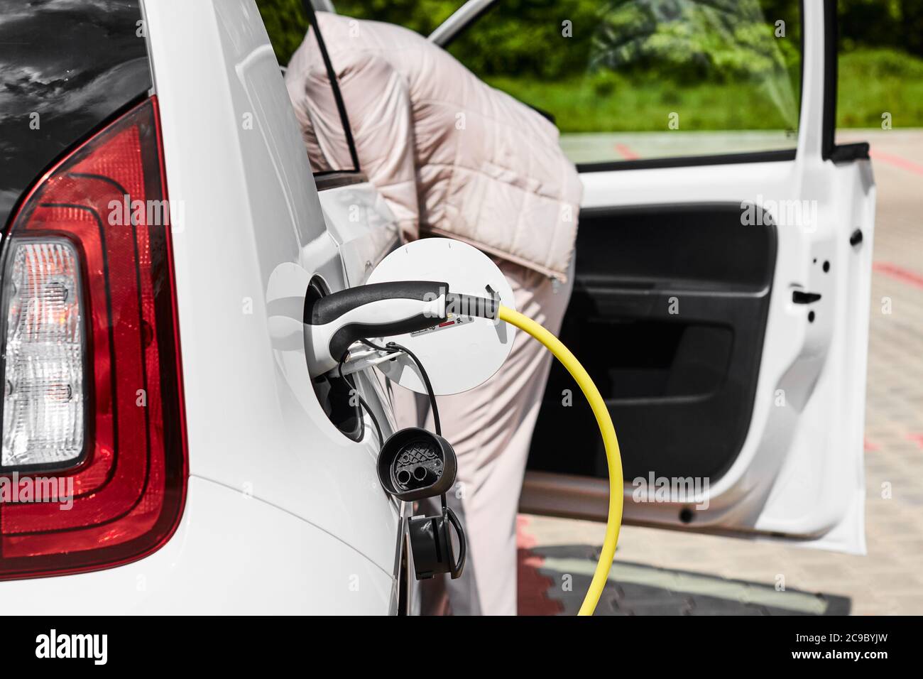 Woman taking something from the car, while electric car is charging at ...