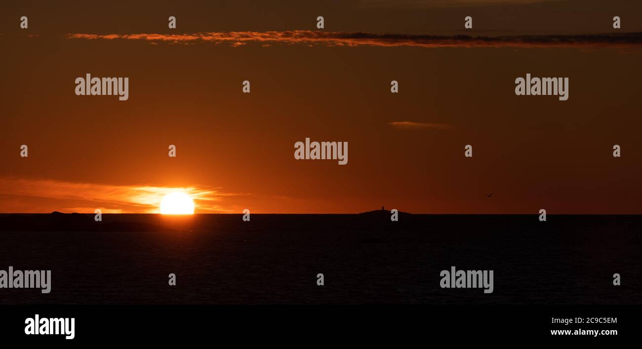 The sun setting in the ocean with small islands and a lighthouse in the ...