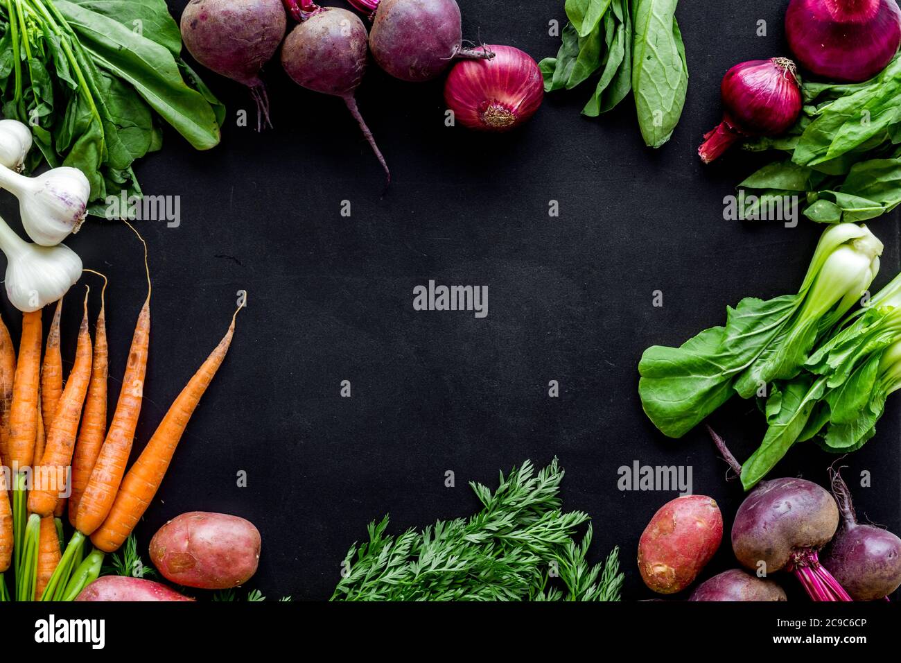 Flat lay of fresh vegetables and greenery on black table top-down copy ...