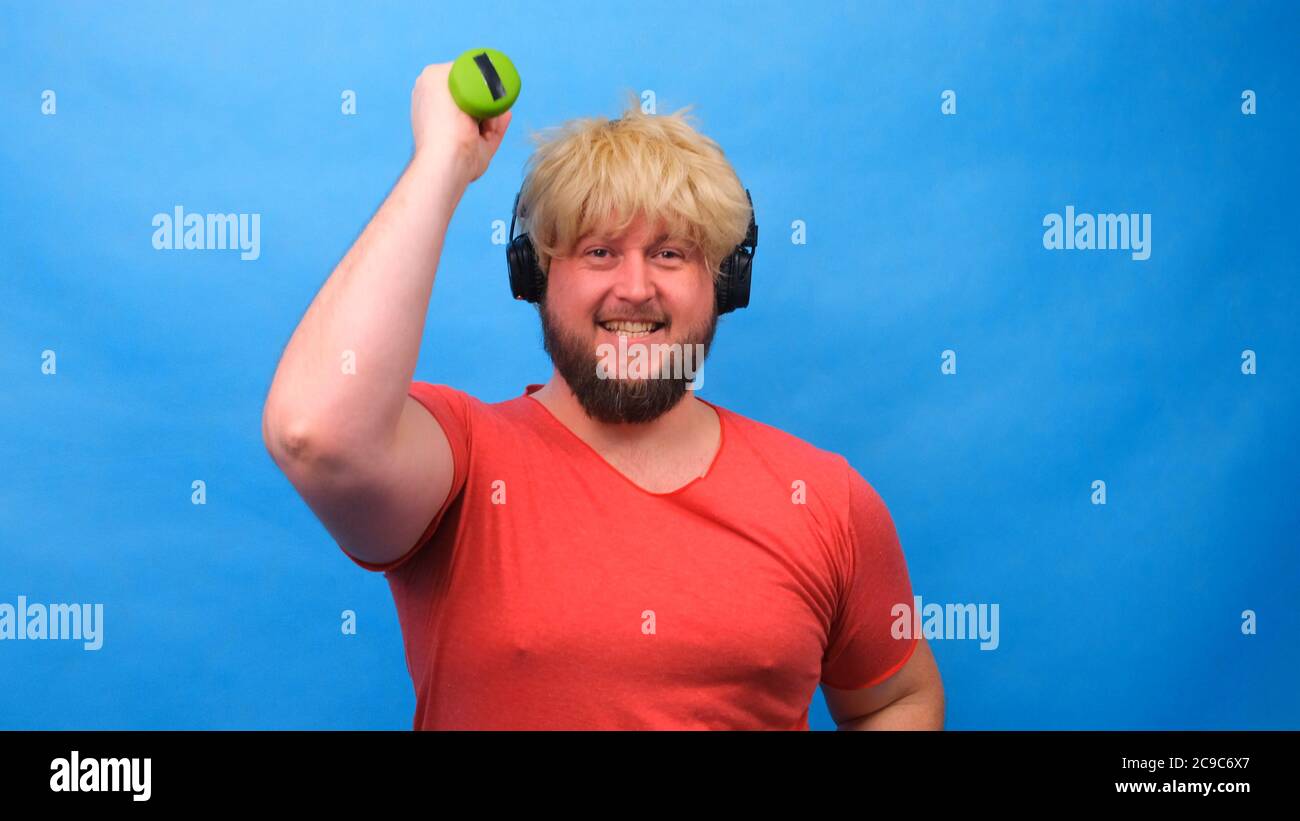 Funny fat man freaky in a wig and a pink t-shirt with dumbbells doing ...