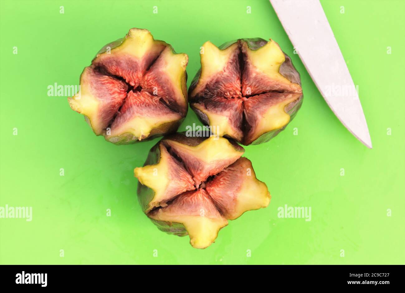 Top down image of three ripe green figs cut open with knife on green ...