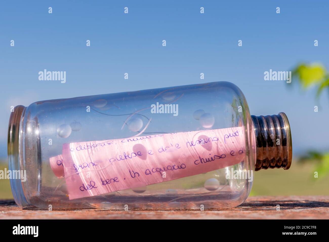 A handwritten letter on a pink sheet is rolled up inside a glass bottle ...