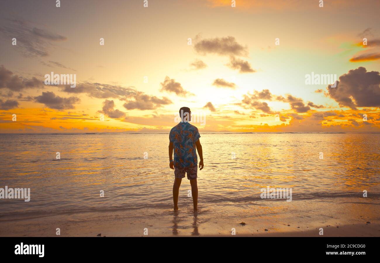 Tropical sunset in front of the ocean on a beautiful island. Man on ...