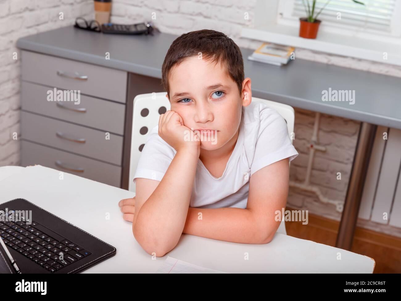 Sad schoolboy sitting alone at desk at home. Grumpy dissatisfied boy ...