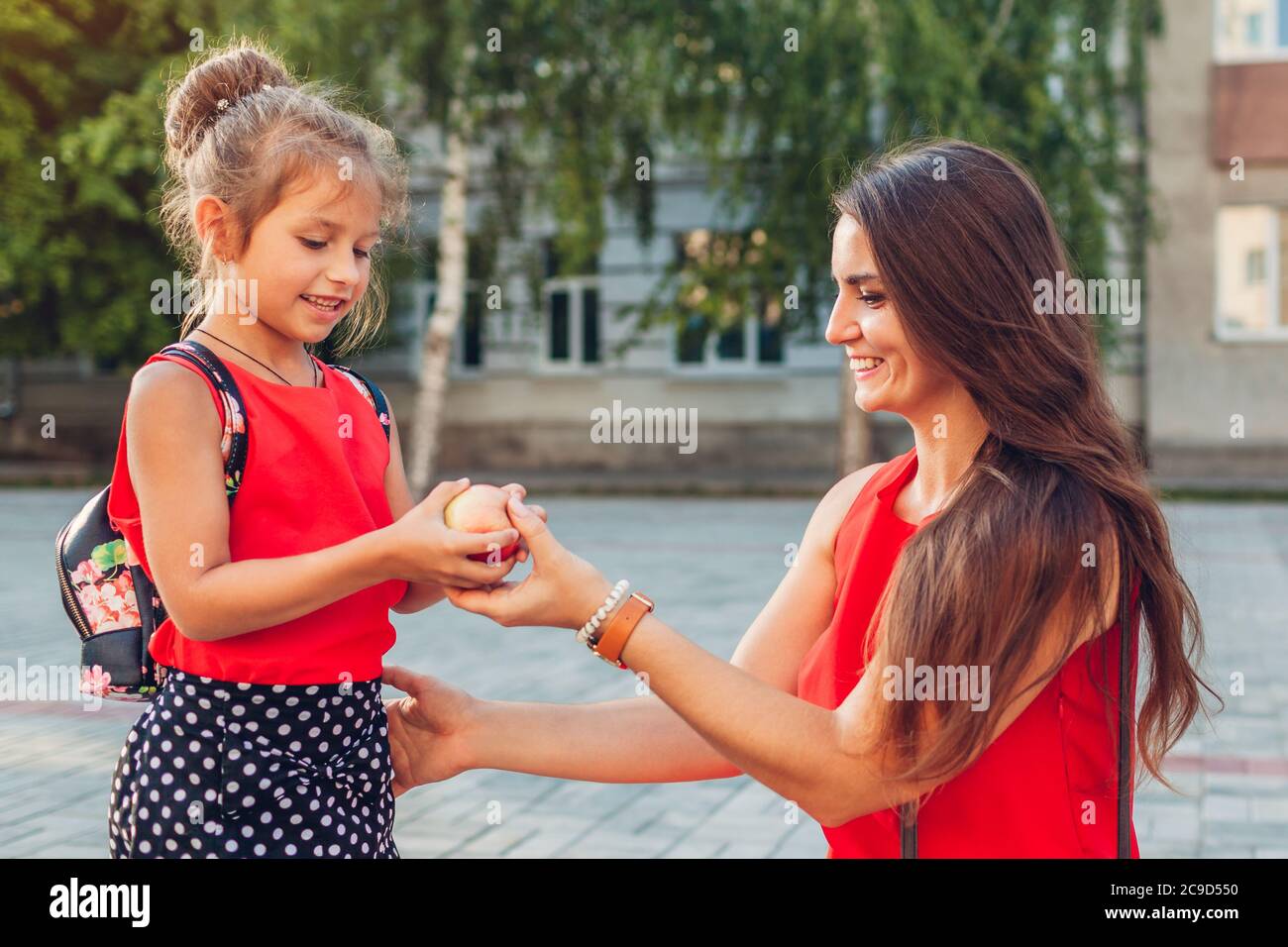 Mother giving little daughter apple outdoors primary school. Little ...