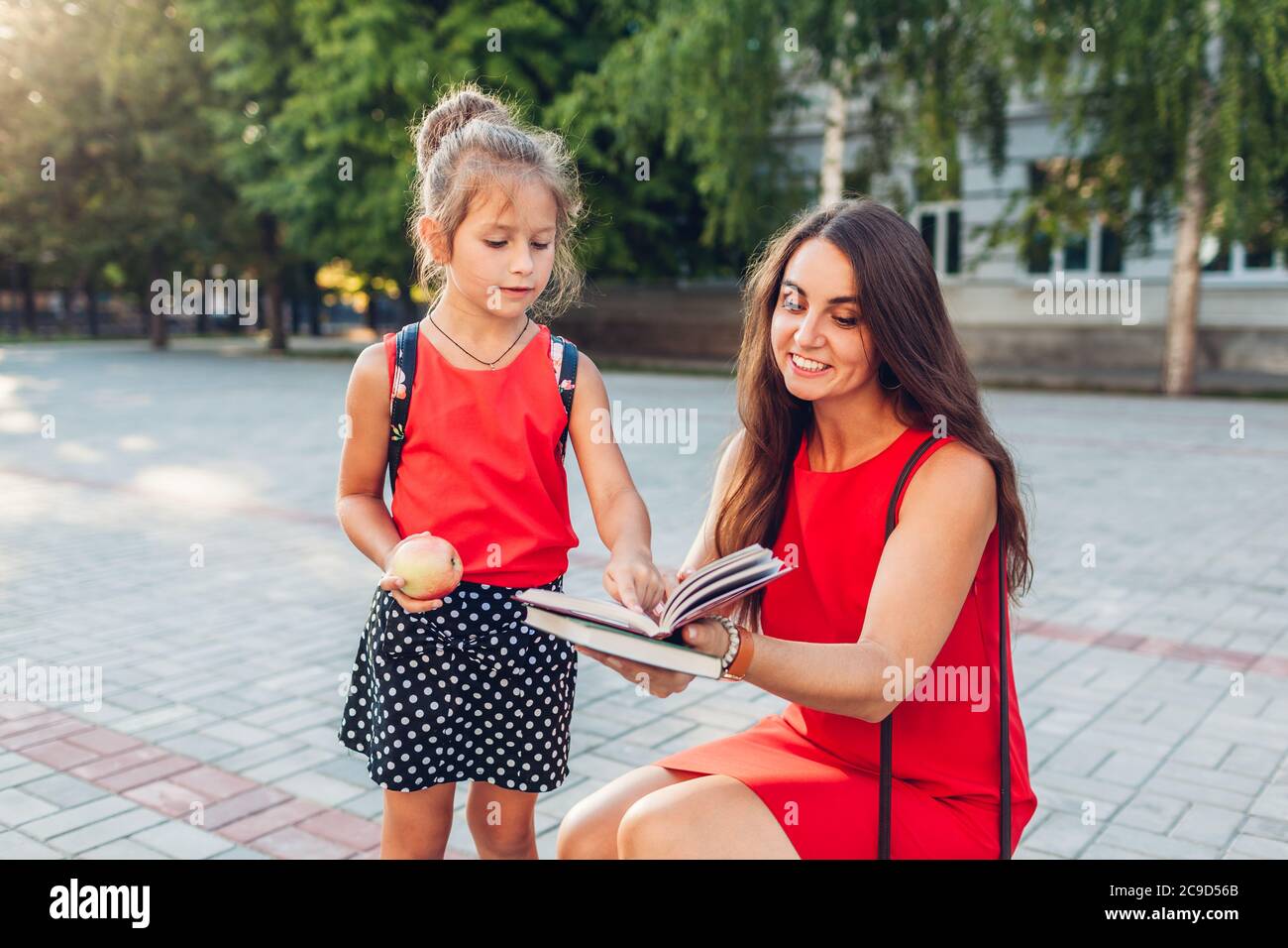 Happy mother and daughter reading book before classes outdoors primary ...