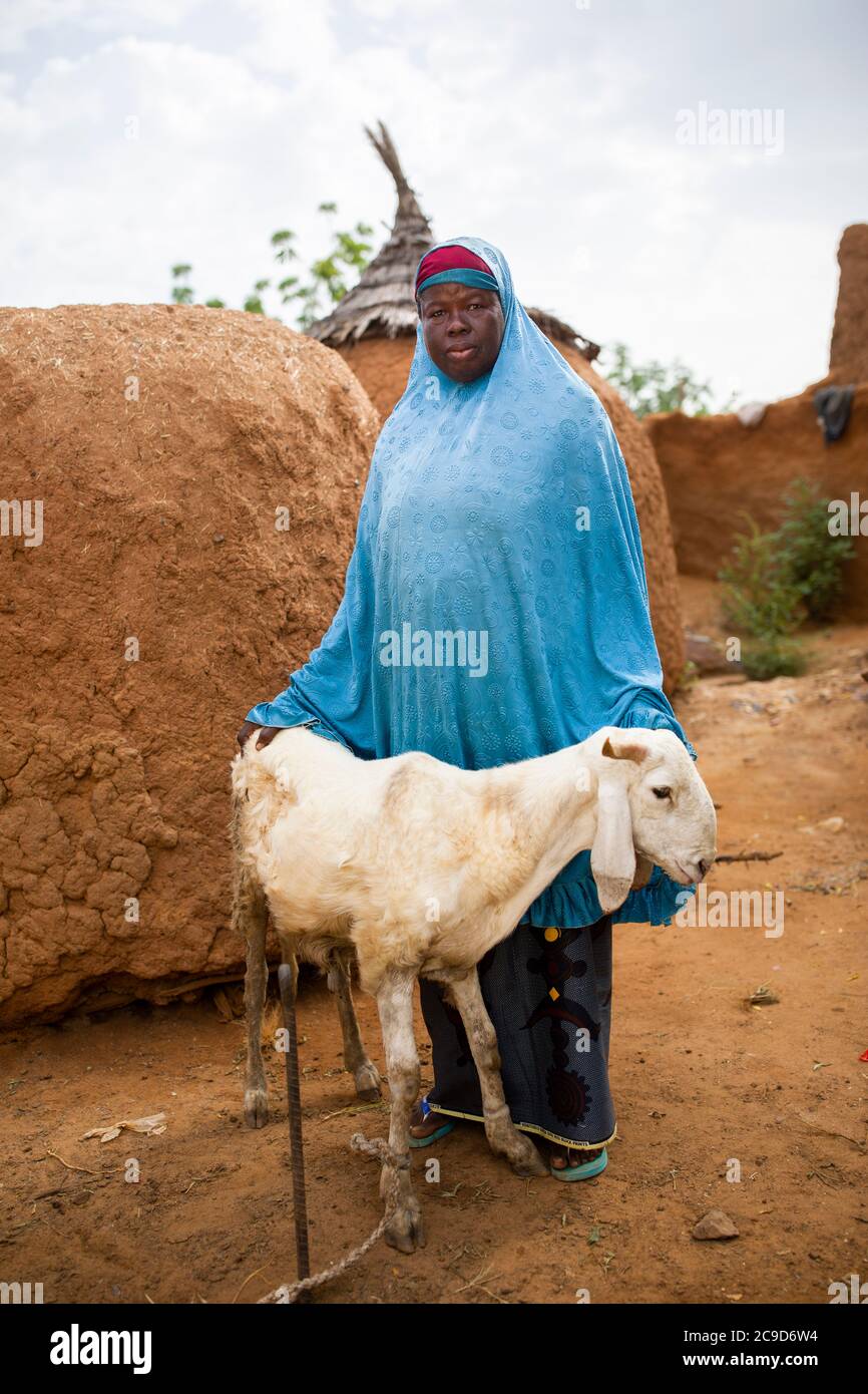 An African woman farmer stands with her sheep outside her traditional ...
