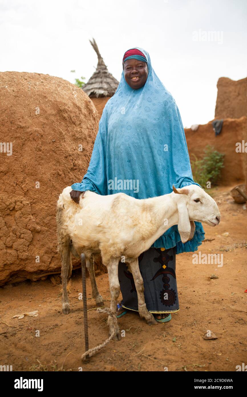 An African woman farmer stands with her sheep outside her traditional ...