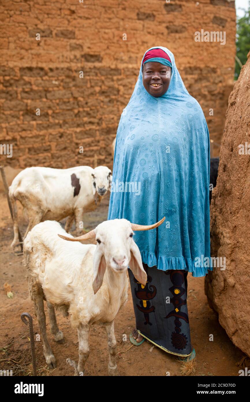 An African woman farmer stands with her sheep outside her traditional ...