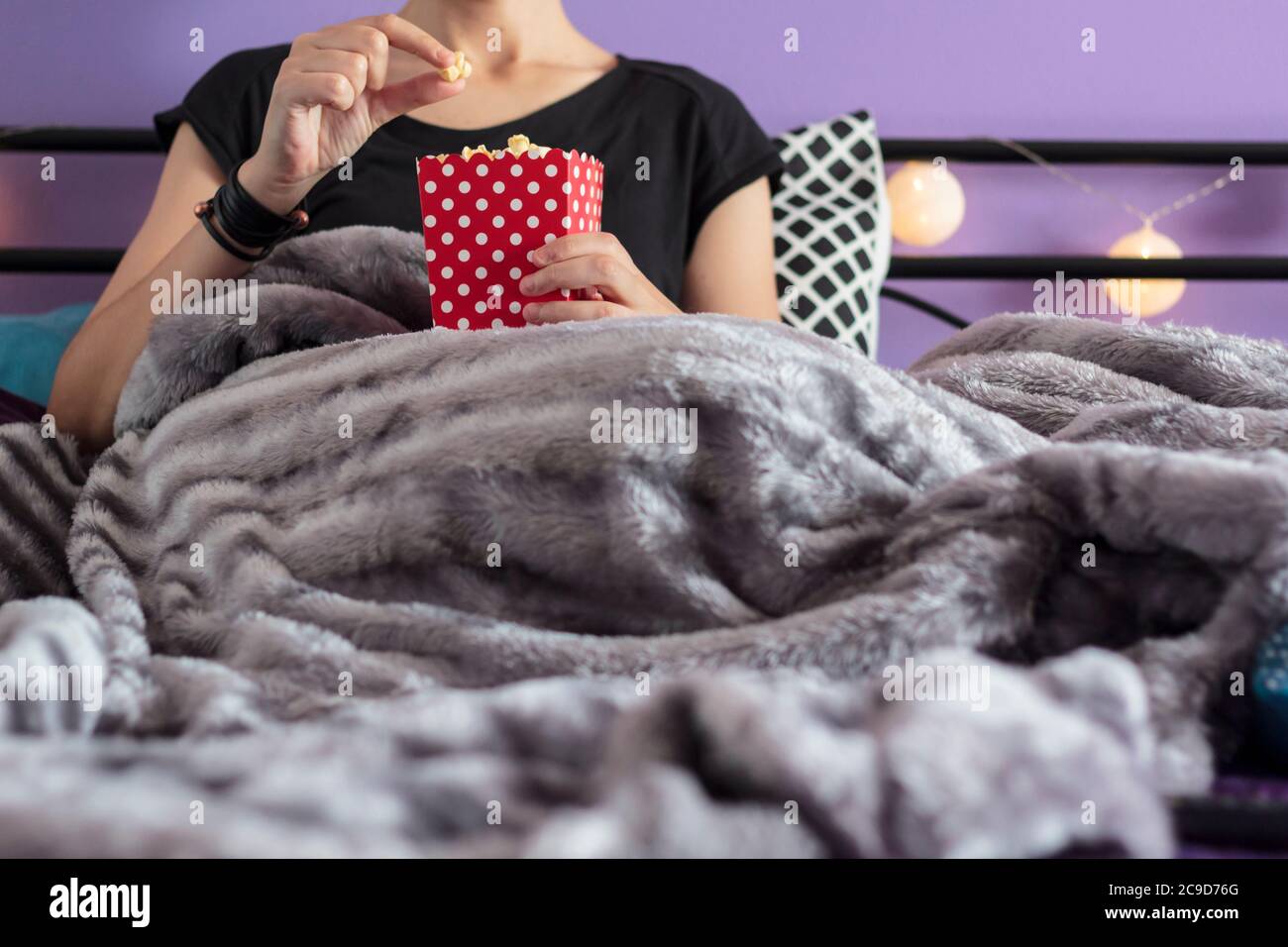 Woman sitting on bed covered with blanket eating popcorn Stock Photo ...