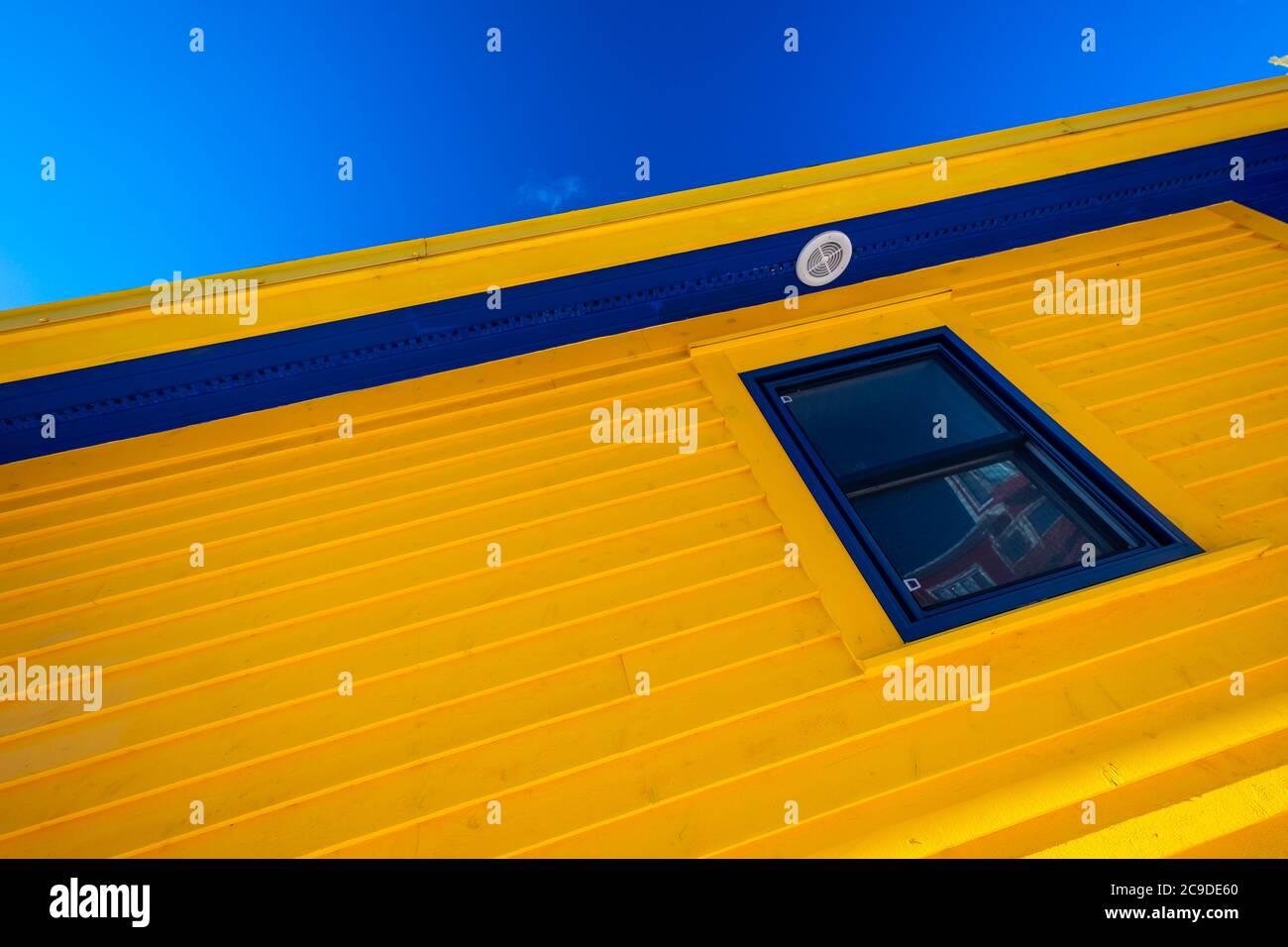 A diagonal view of a bright yellow vintage wooden building with purple ...