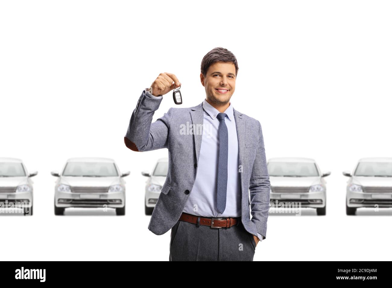 Young man with car keys posing in front of cars in a showroom isolated ...