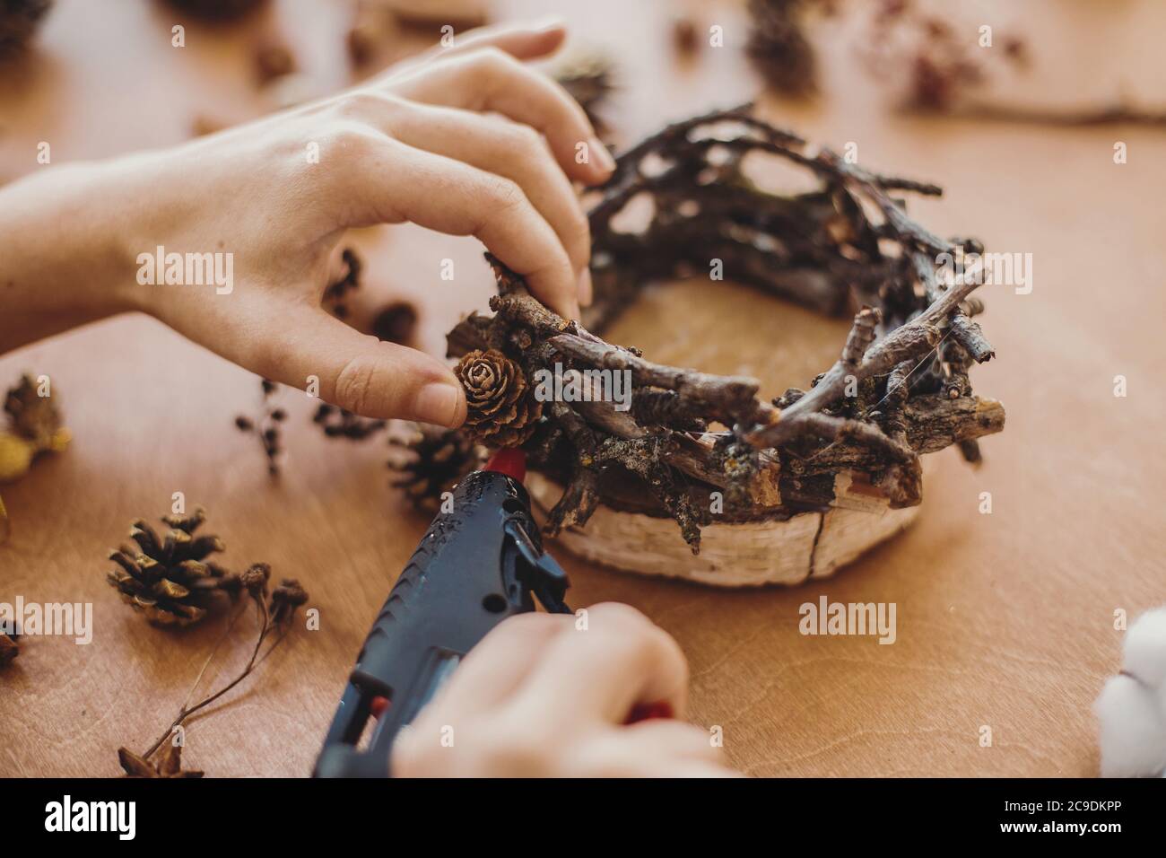 Hands holding glue gun and making rustic festive decoration from pine ...