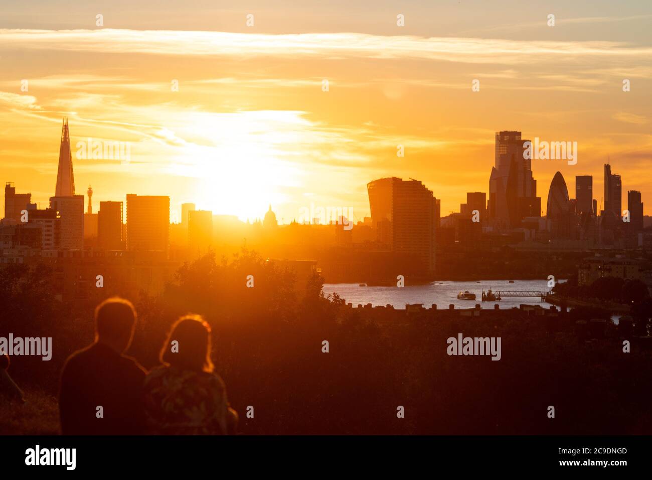 People watch the sun set behind the London skyline from Greenwich Park ...