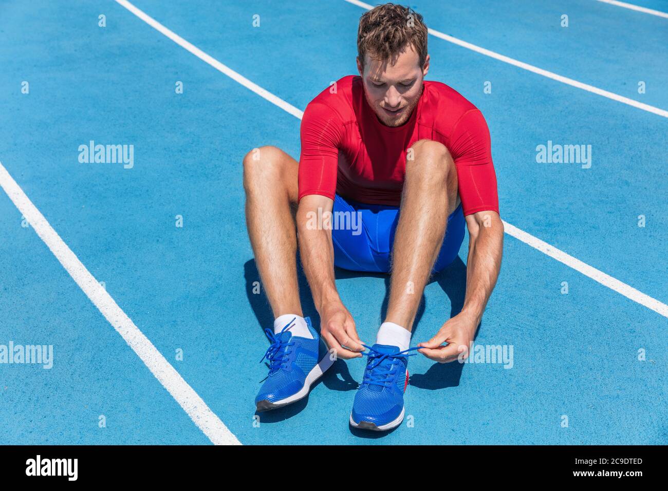 Athlete sprinter getting ready to run tying up shoe laces on stadium ...
