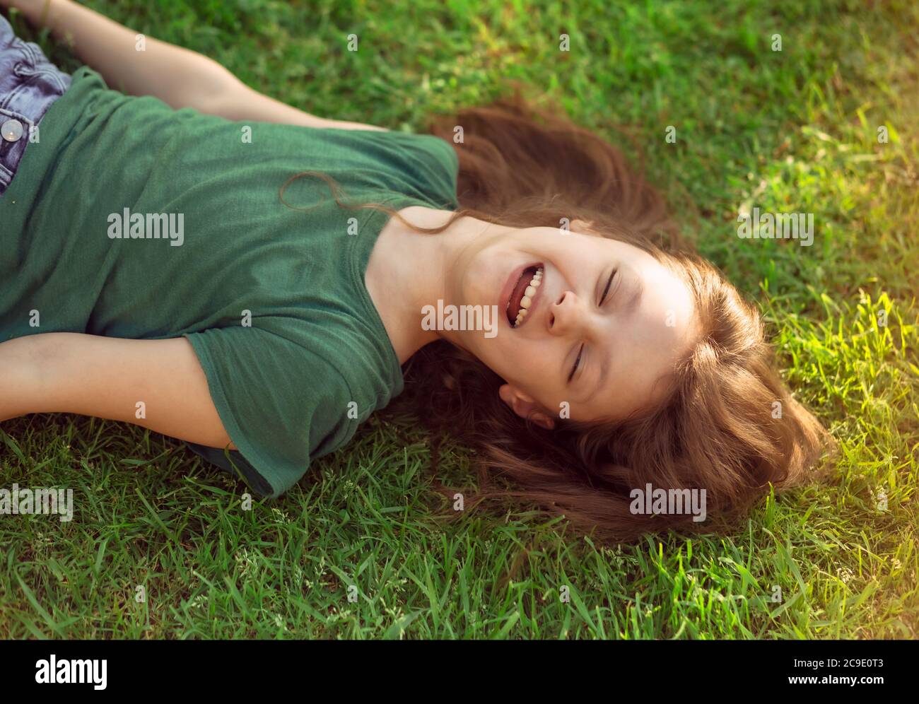 Happy laughing fun kid girl lying on the grass on nature summer ...