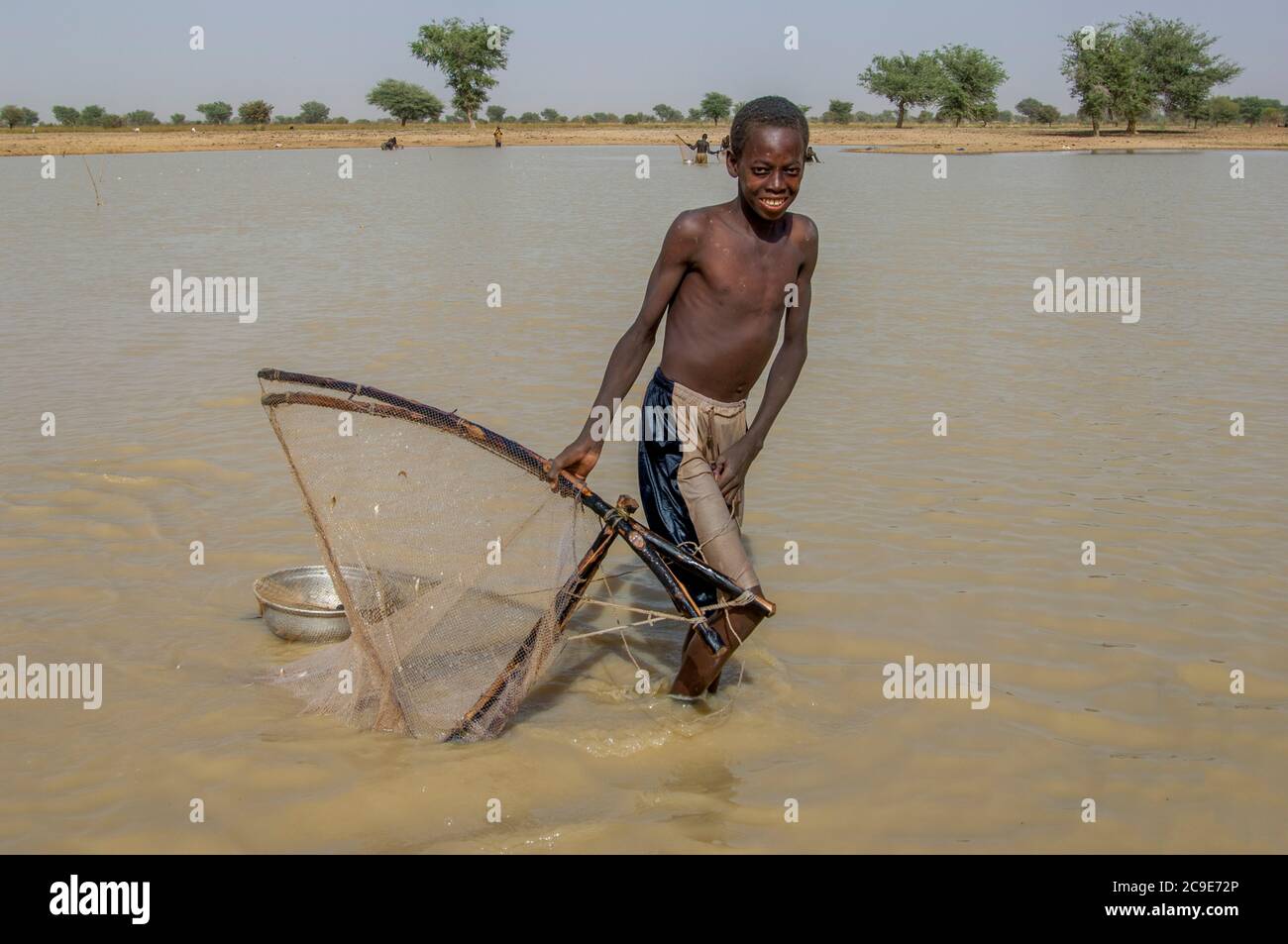 A teenage boy is fishing with a net in a pond near Djenne, a town in ...