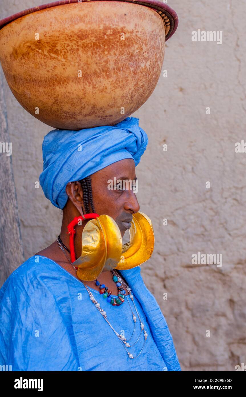 A Fulani tribal woman with festive gold earrings and tattooed lips ...