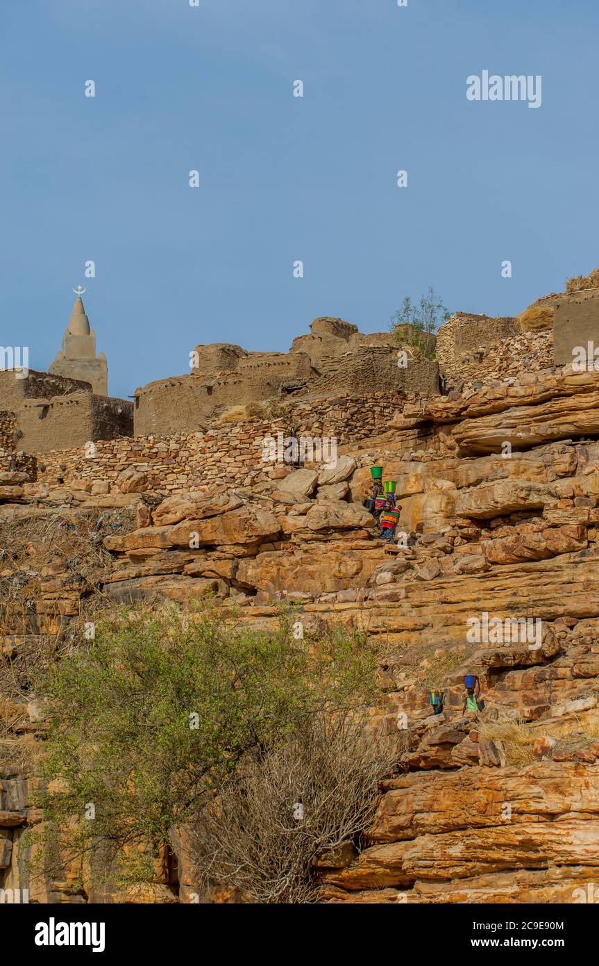 Women carrying buckets with water on their heads up to the Niogono ...